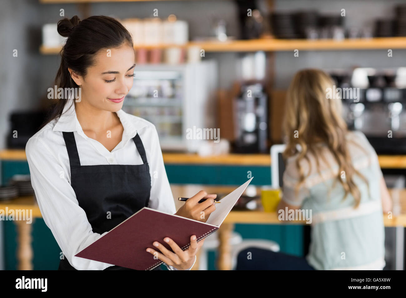 Smiling waitress writing in a file Stock Photo - Alamy