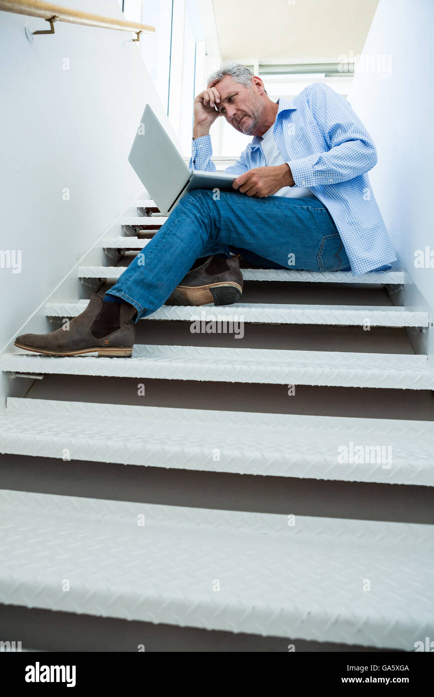 Tensed man using laptop on steps Stock Photo - Alamy