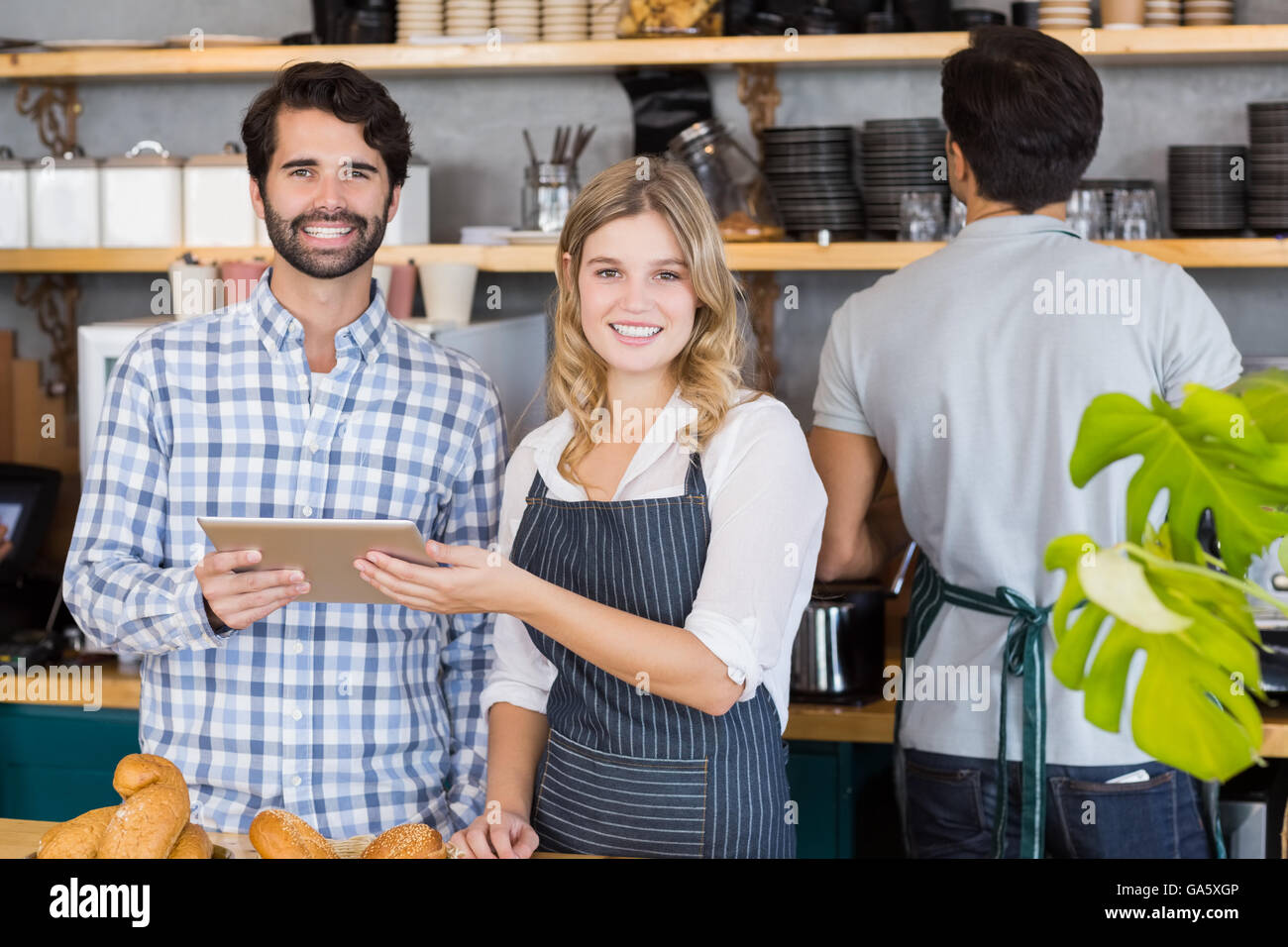 Smiling man and waitresses standing at counter using digital tablet ...