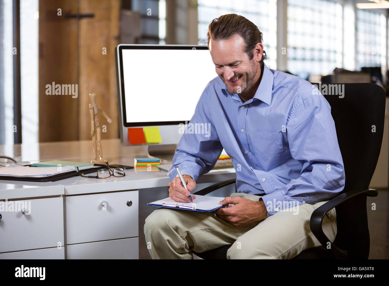 Businessman smiling while writing on clipboard Stock Photo - Alamy