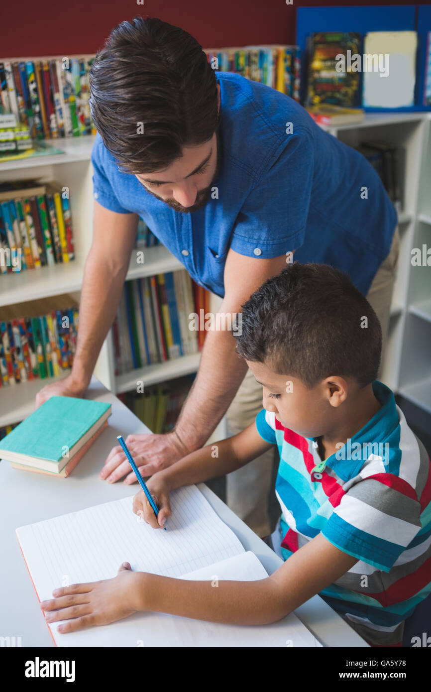 Teacher helping school kid with his homework in library Stock Photo - Alamy
