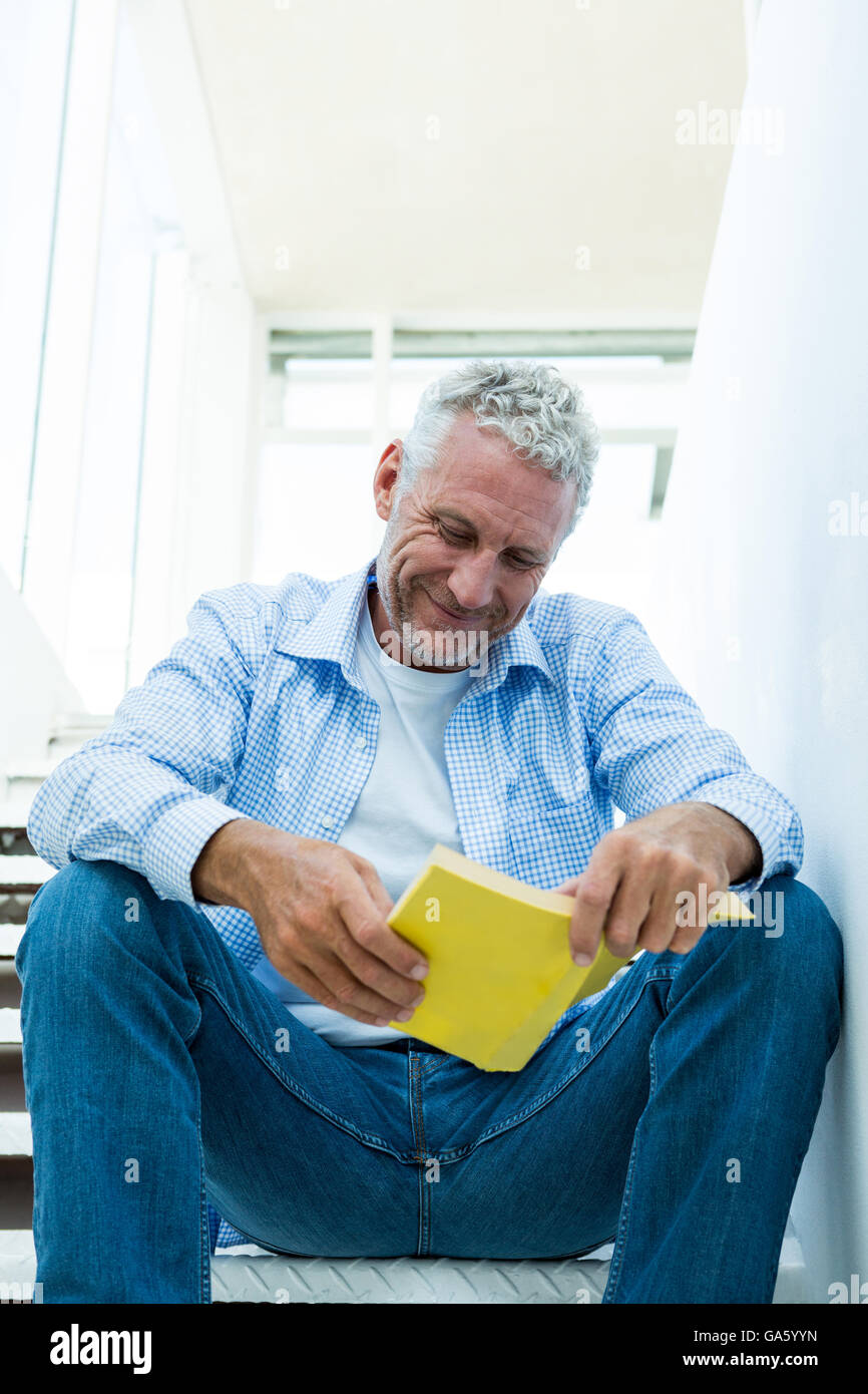 Smiling man reading book on steps Stock Photo - Alamy
