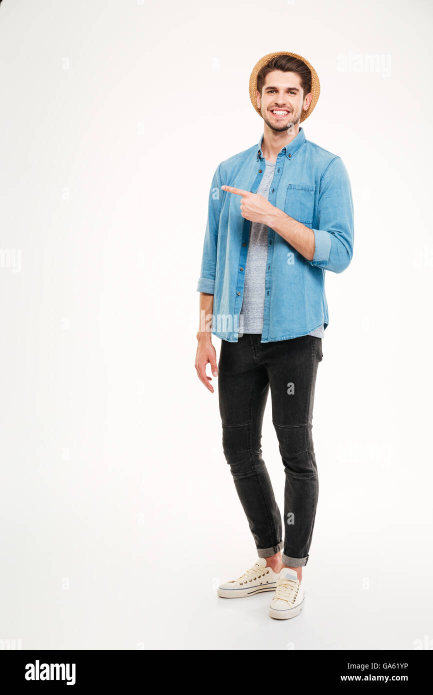 Handsome young man pointing away and smiling while standing against ...