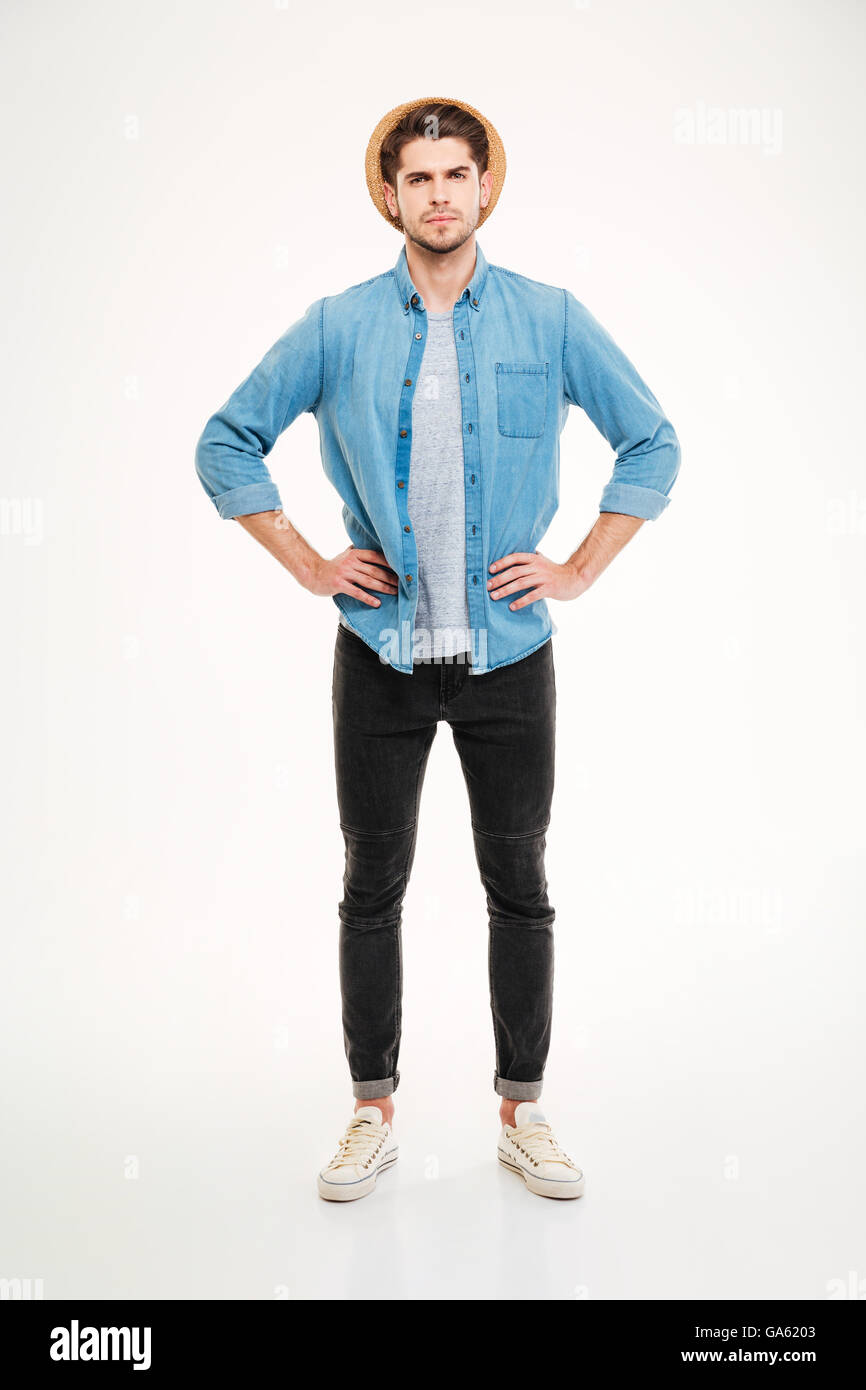 Serious strict young man standing with hands on waist over white ...