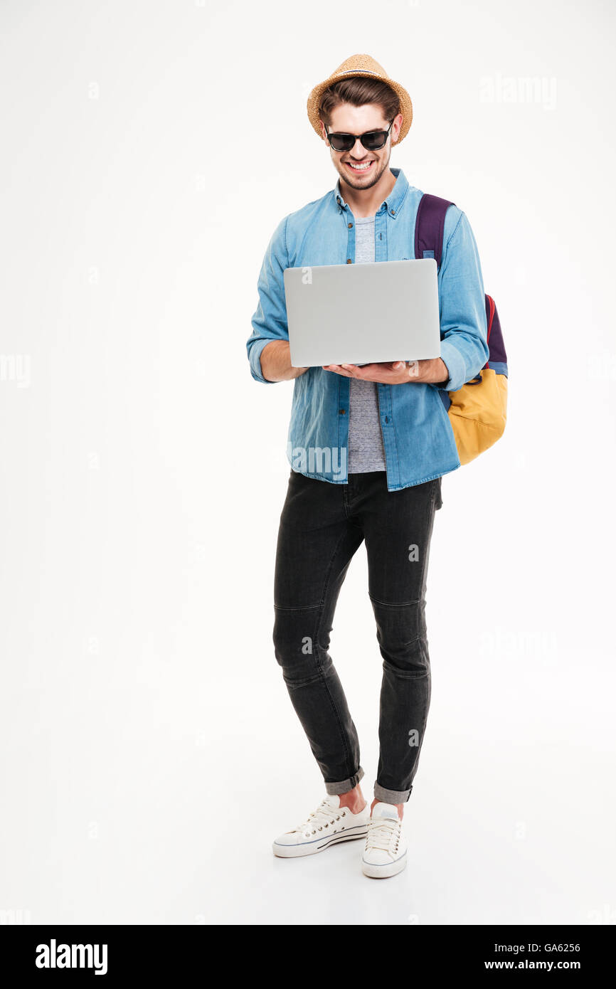 Happy handsome young man with backpack standing and using laptop Stock ...