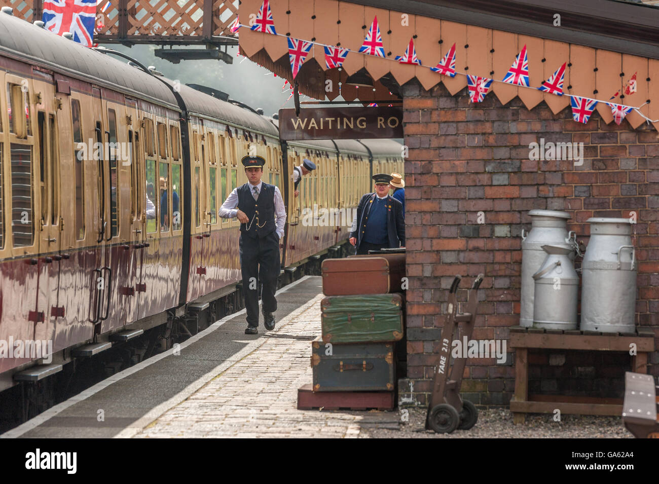 A train guard walking along the platform next to a steam train Stock ...