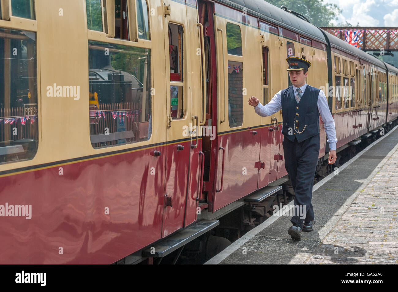 A train guard walking along the platform next to a steam train Stock ...