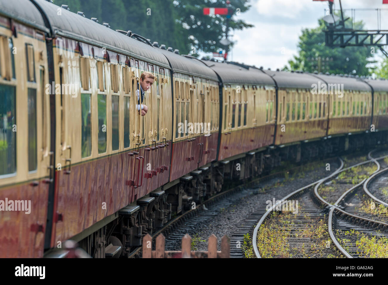 A steam train pulling out of the platform with a guard looking out the ...