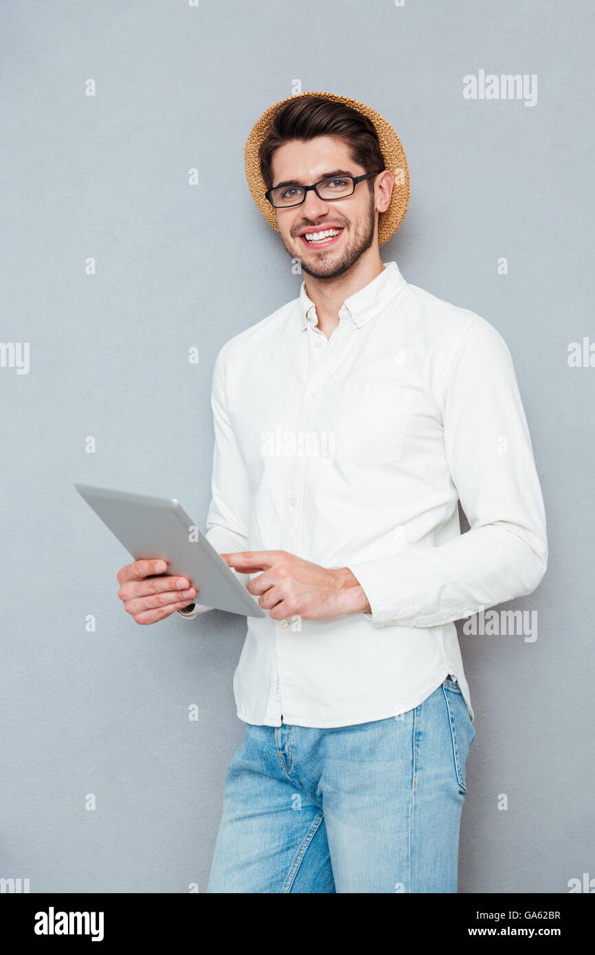 Portrait of a happy young man using tablet computer isolated on a gray ...