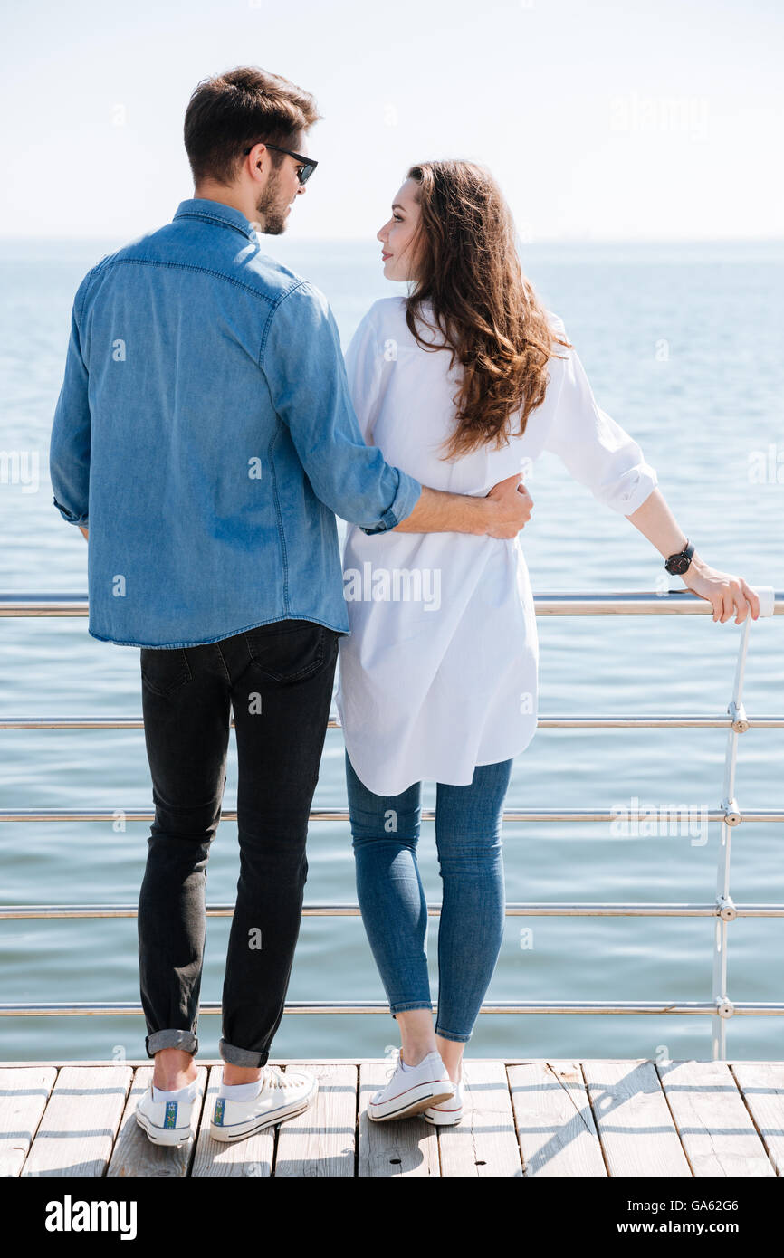 Full length of a young couple standing backwards hugging and looking at ...