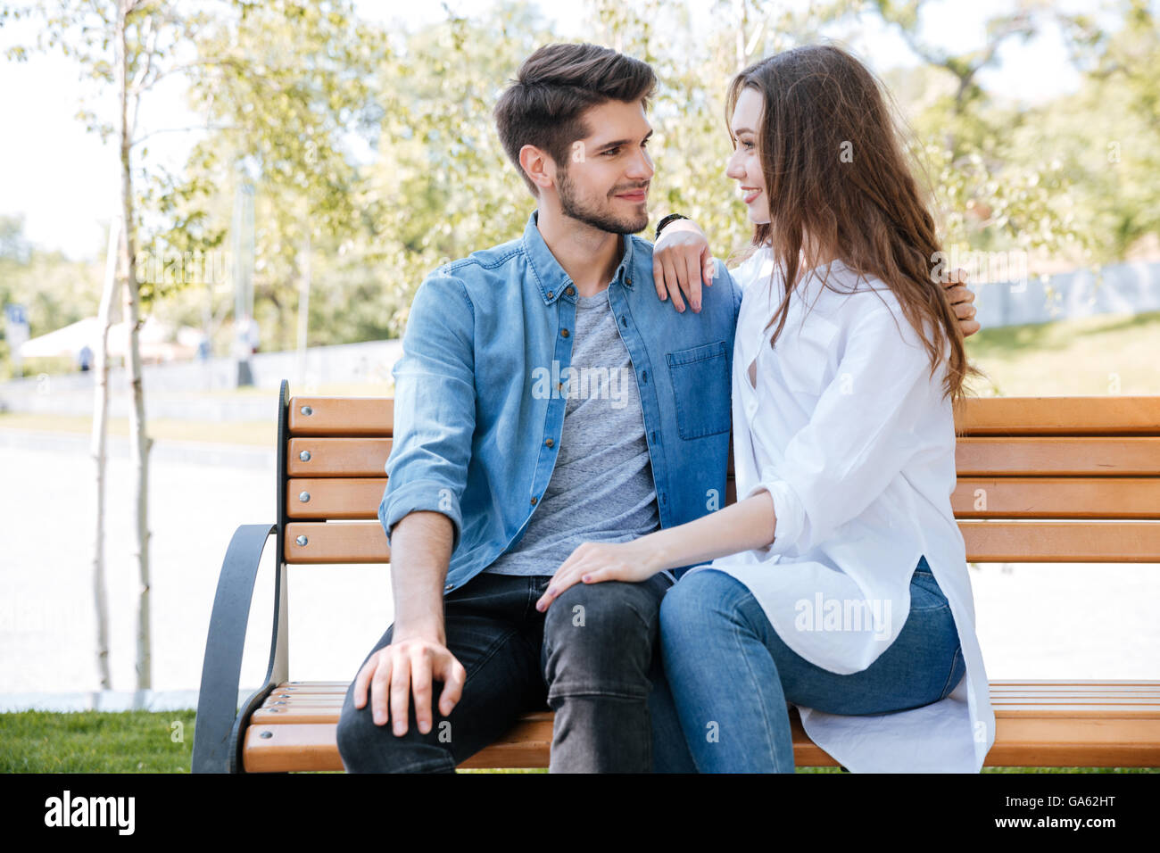 Happy young beautiful couple in love sitting on a park bench and ...