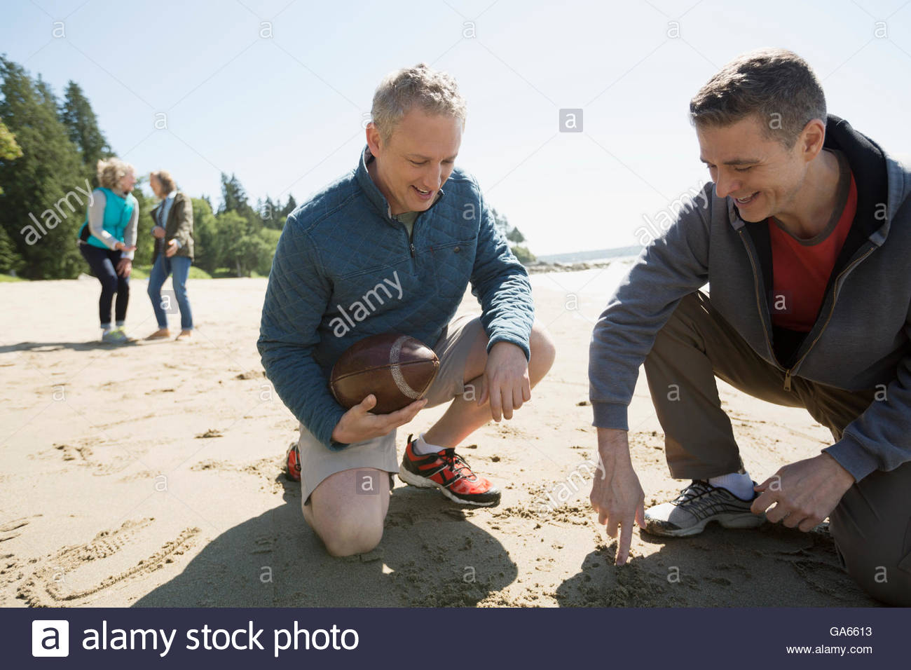 Men playing football drawing game plan in sand on sunny beach Stock ...