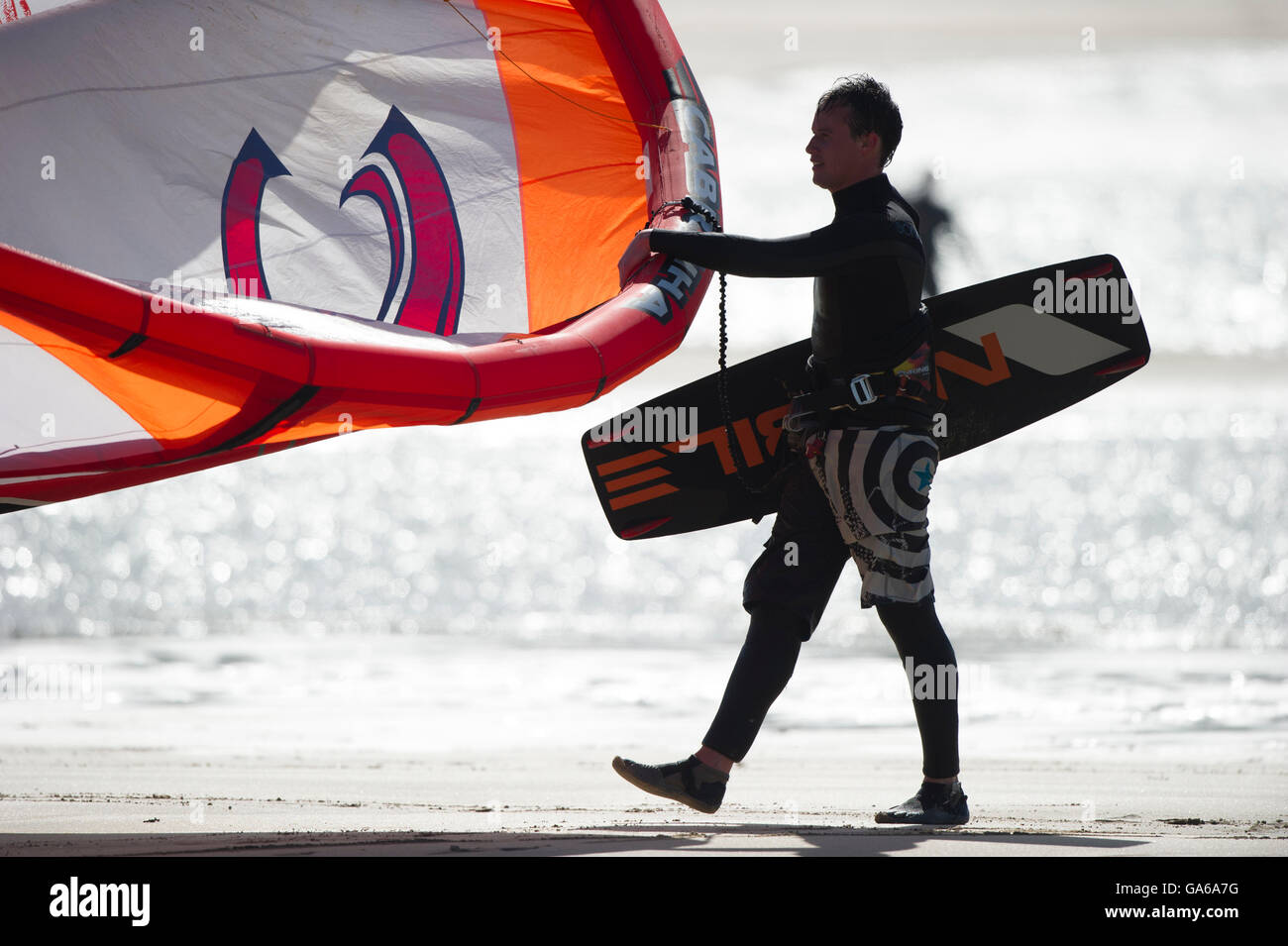 Kite surfer carrying board and inflated colourful orange red and white ...