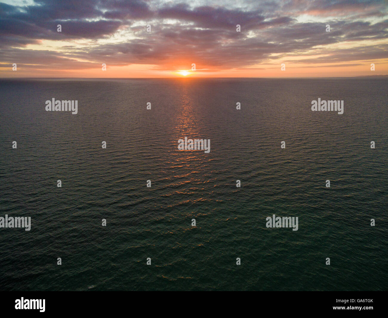 Orange sunset over water with sun peeking out of the clouds Stock Photo ...