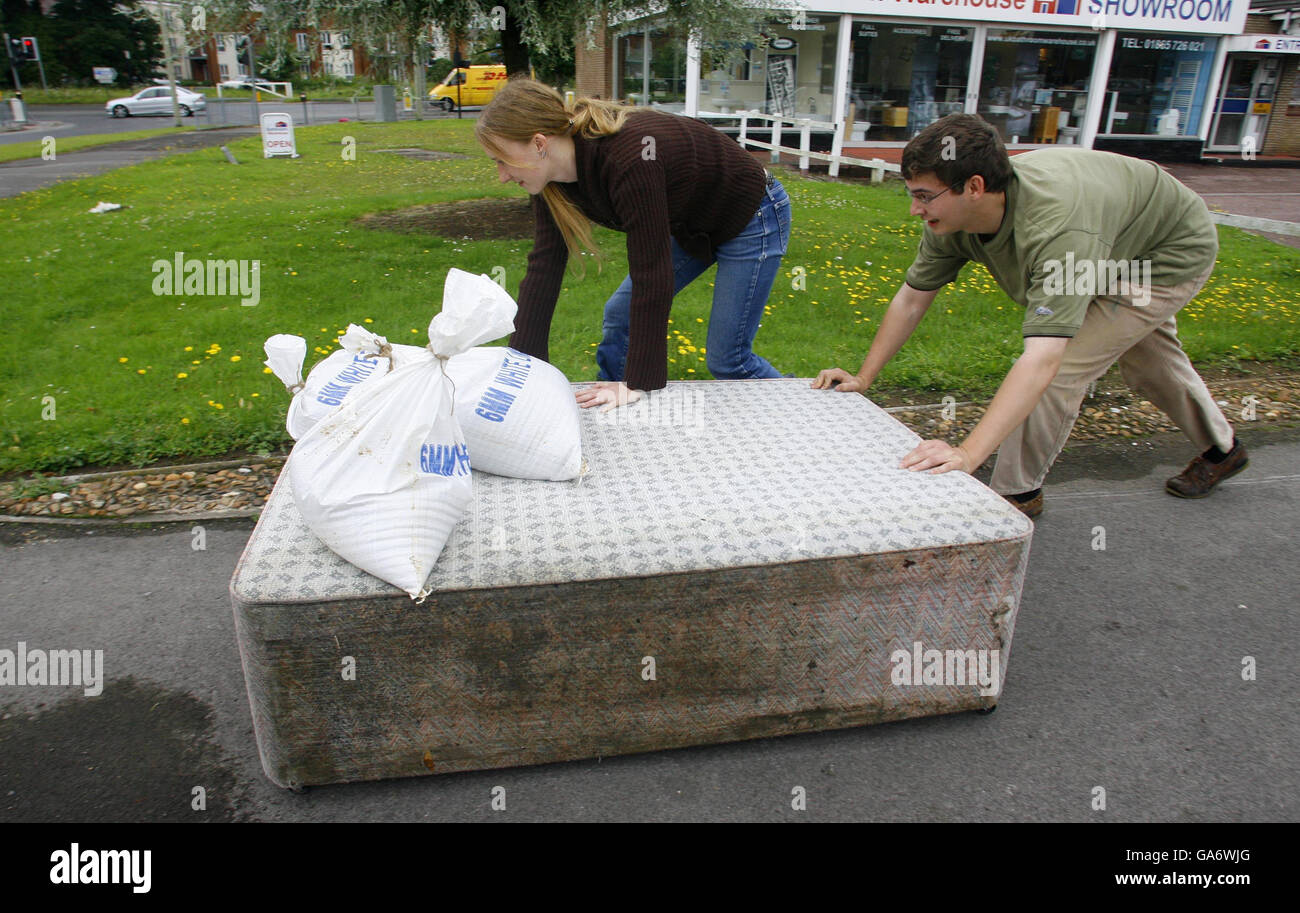A young couple use an old bed to move heavy sandbags to their home on ...