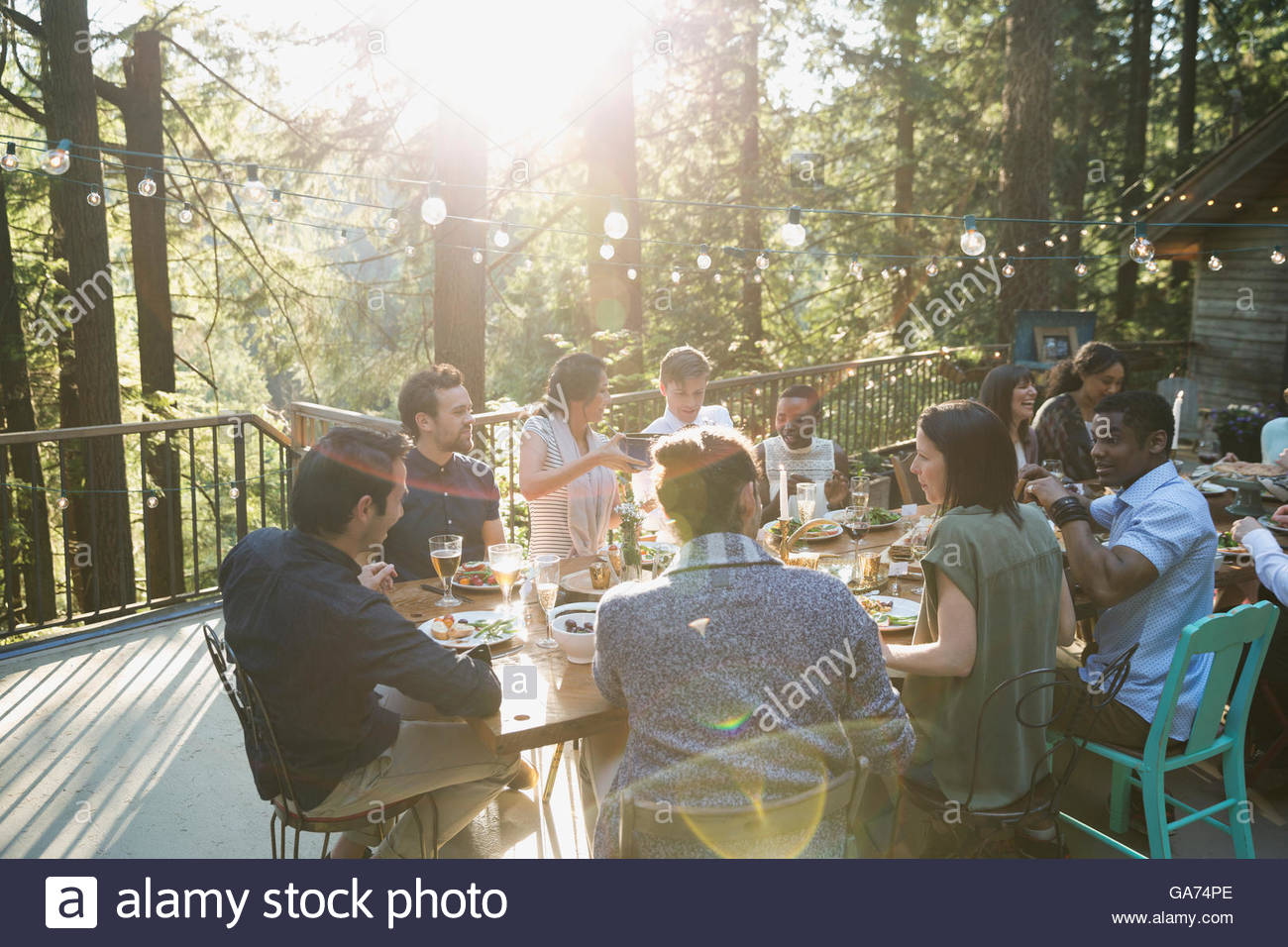 Friends dining around long dining table on balcony at wedding reception ...
