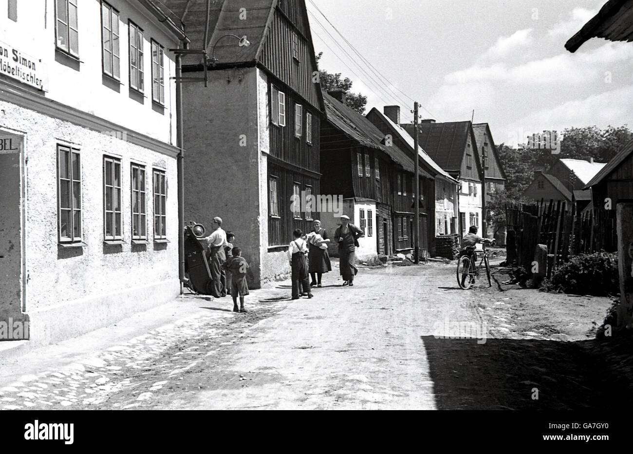 1930s, historical, rural village scene, a woman walks carrying her baby ...