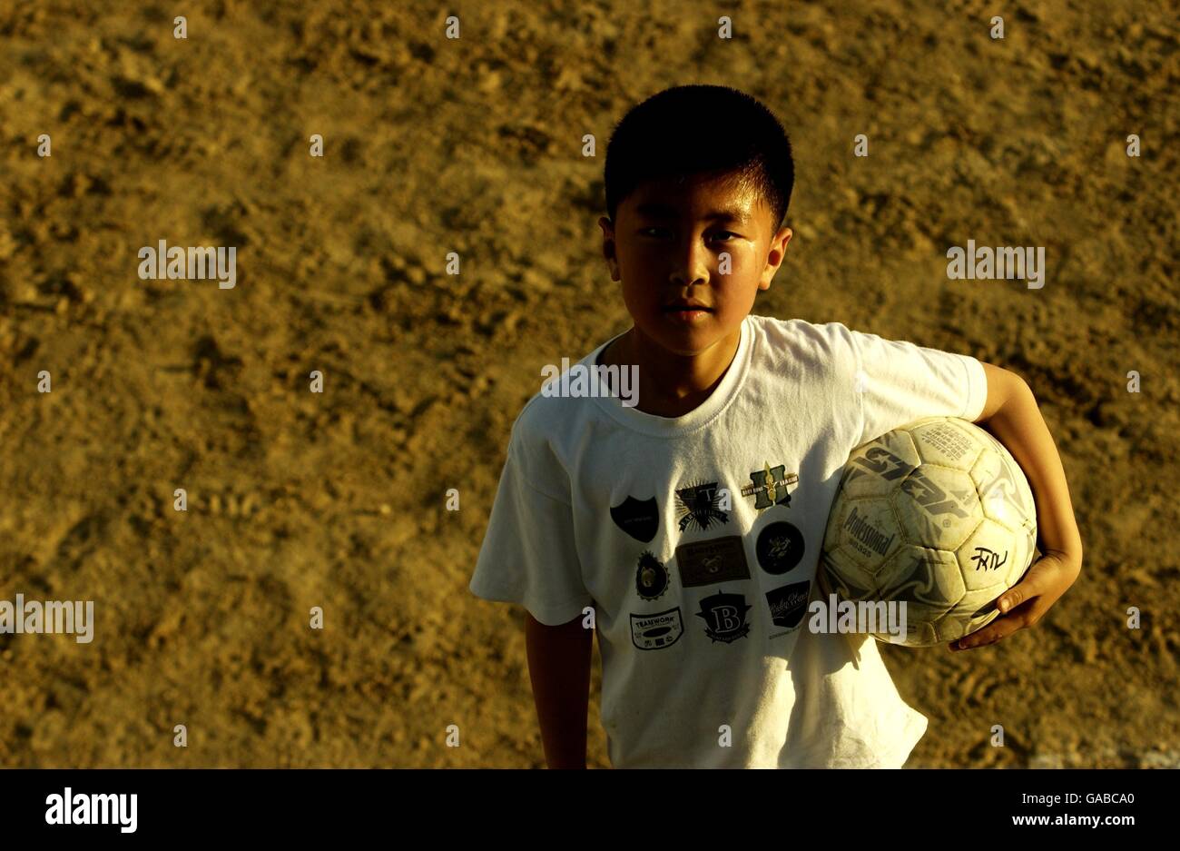 A young boy with a football on a sand football pitch on the island of ...