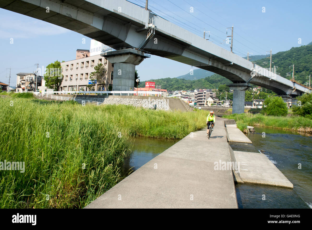 A touring cyclist crossing a river under a railway bridge in Japan ...