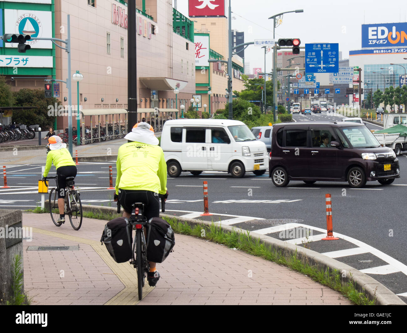 Two touring cyclists cycling on the footpath of a busy intersection ...