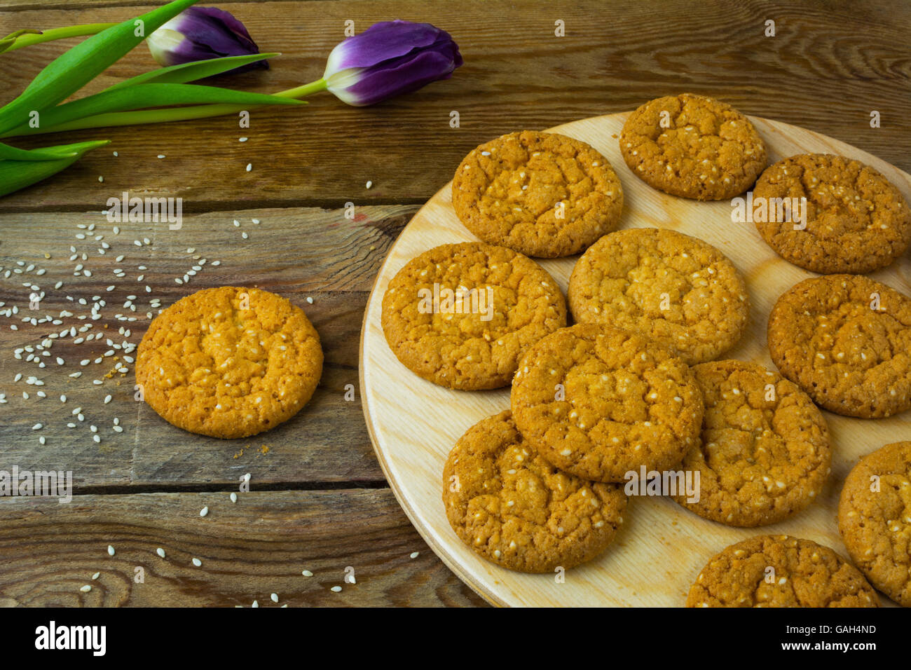 Homemade sesame cookies and two purple tulips on rustic background ...