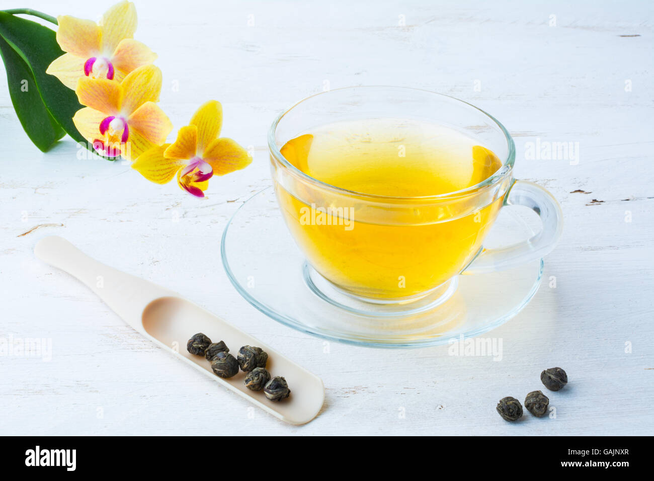 Cup of tea and leaves of green tea braided in balls on white wooden ...