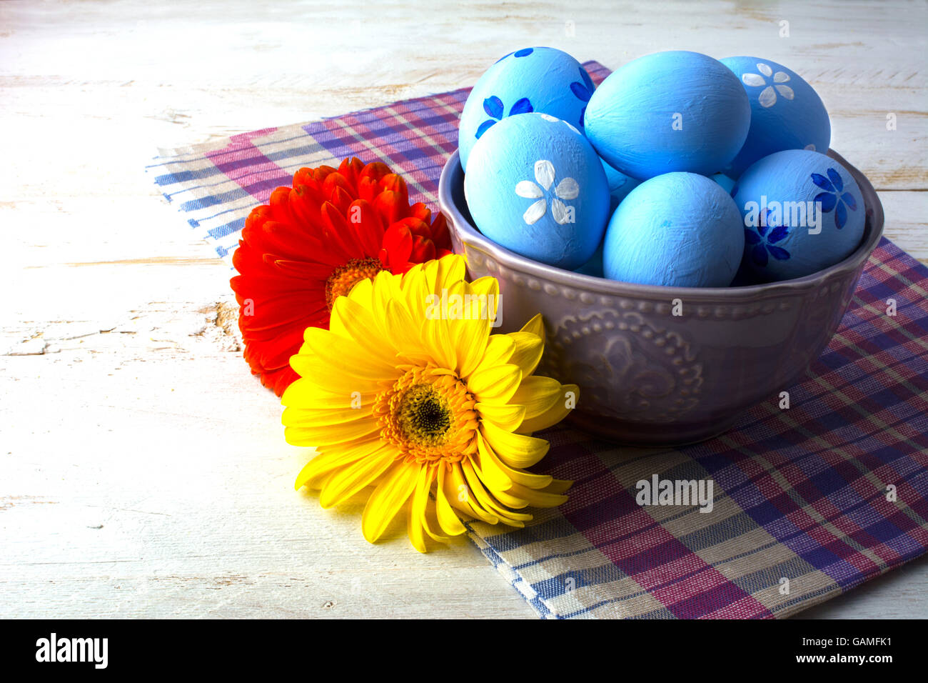 Blue Easter eggs in a purple bowl and flower on a white wooden ...