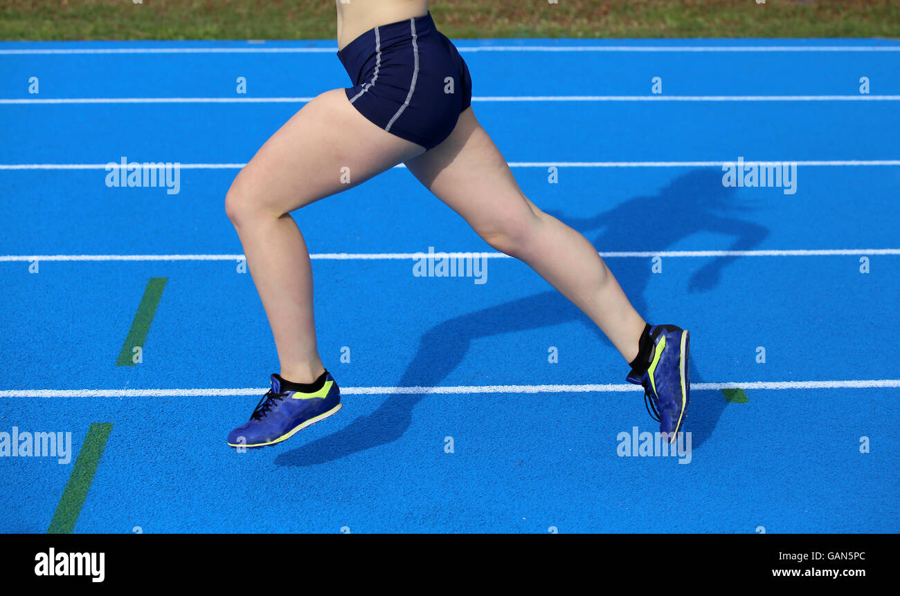long legs of young female runner running on athletic track with blue ...