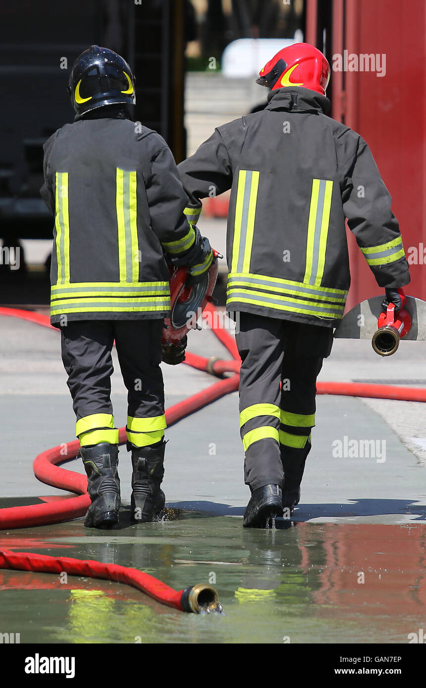 two firefighters carry the hydrant and hose pipes after switching off ...