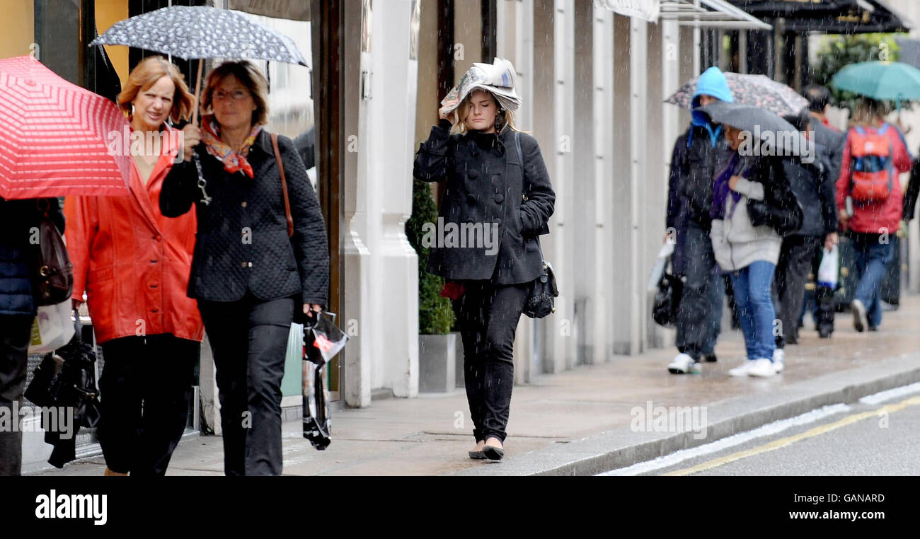 A woman uses a newspaper for cover from heavy rain fall in central ...