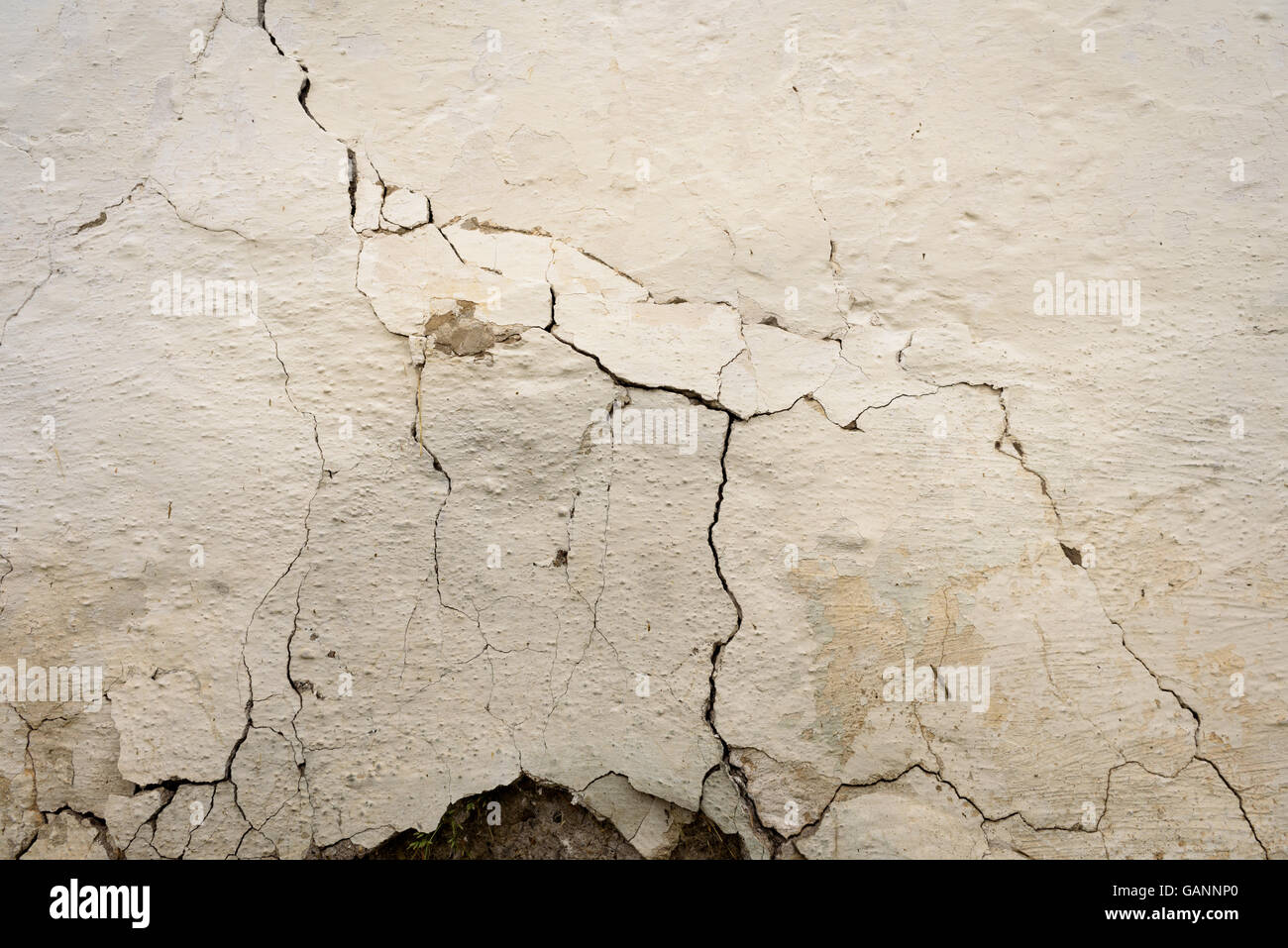 Cracked white painted wall with large fissures on the mottled shaded ...