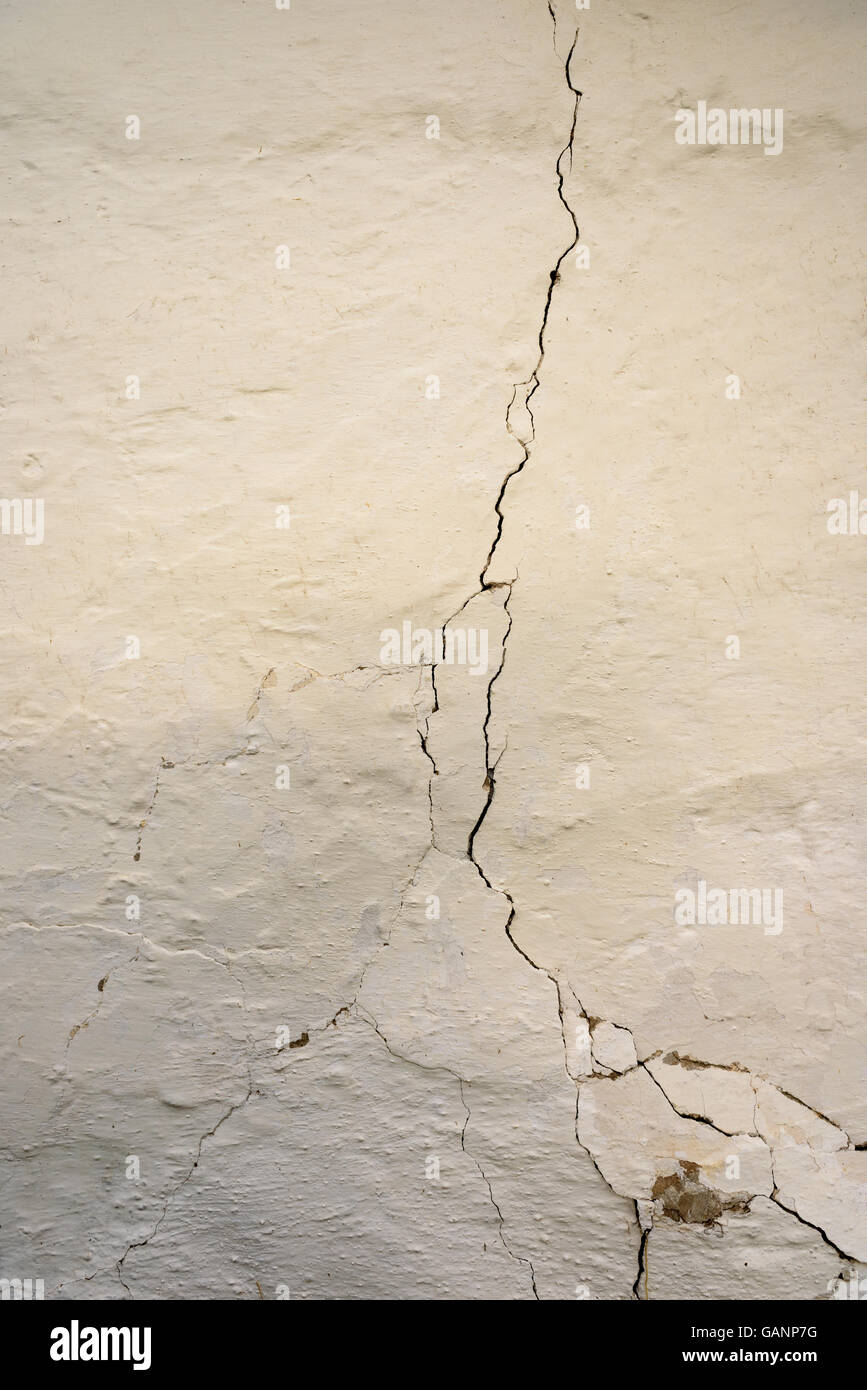 Cracked white painted wall with large fissures on the mottled shaded ...