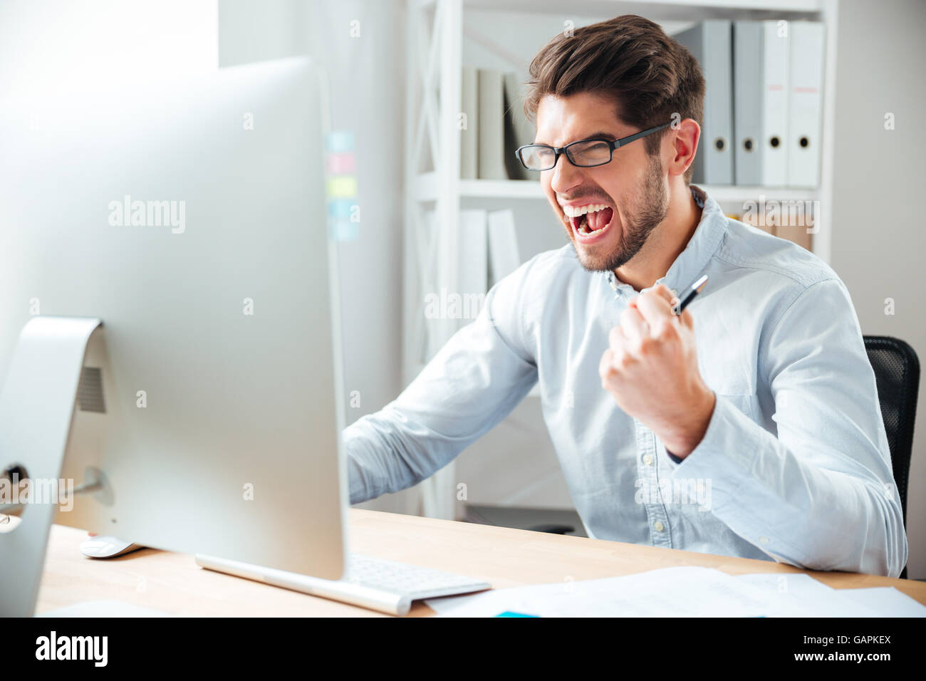 Crazy furious young businessman working and screaming at workplace ...