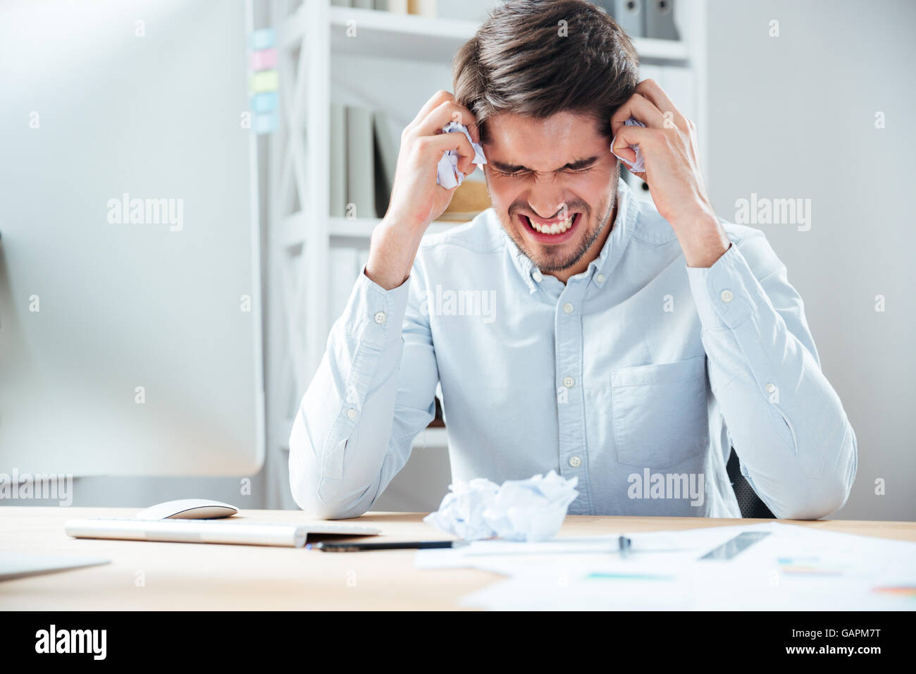 Aggressive angry young businessman holding crumpled paper sitting at ...