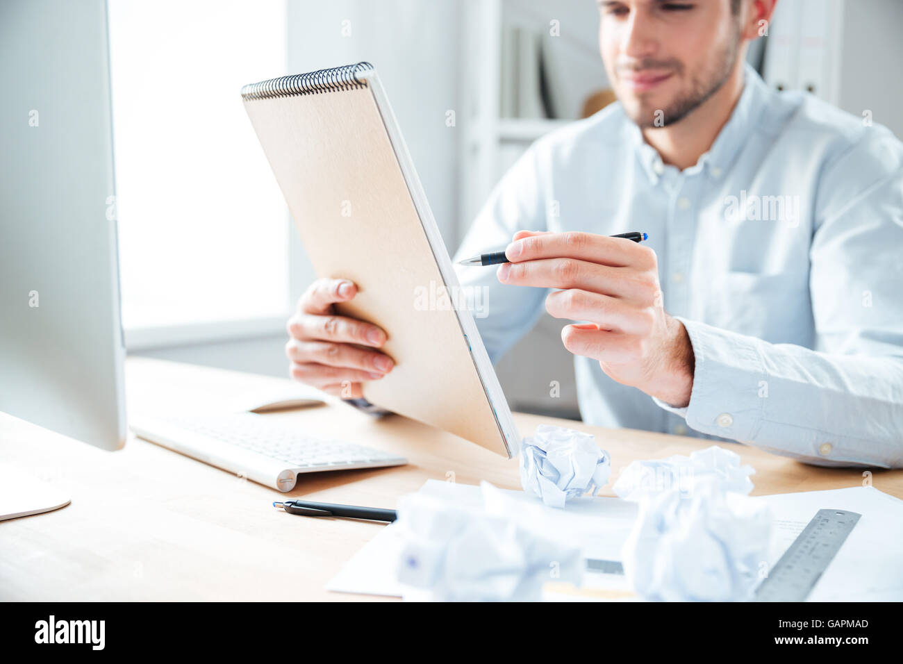 Closeup of smiling young businessman sitting and writing in notepad at ...