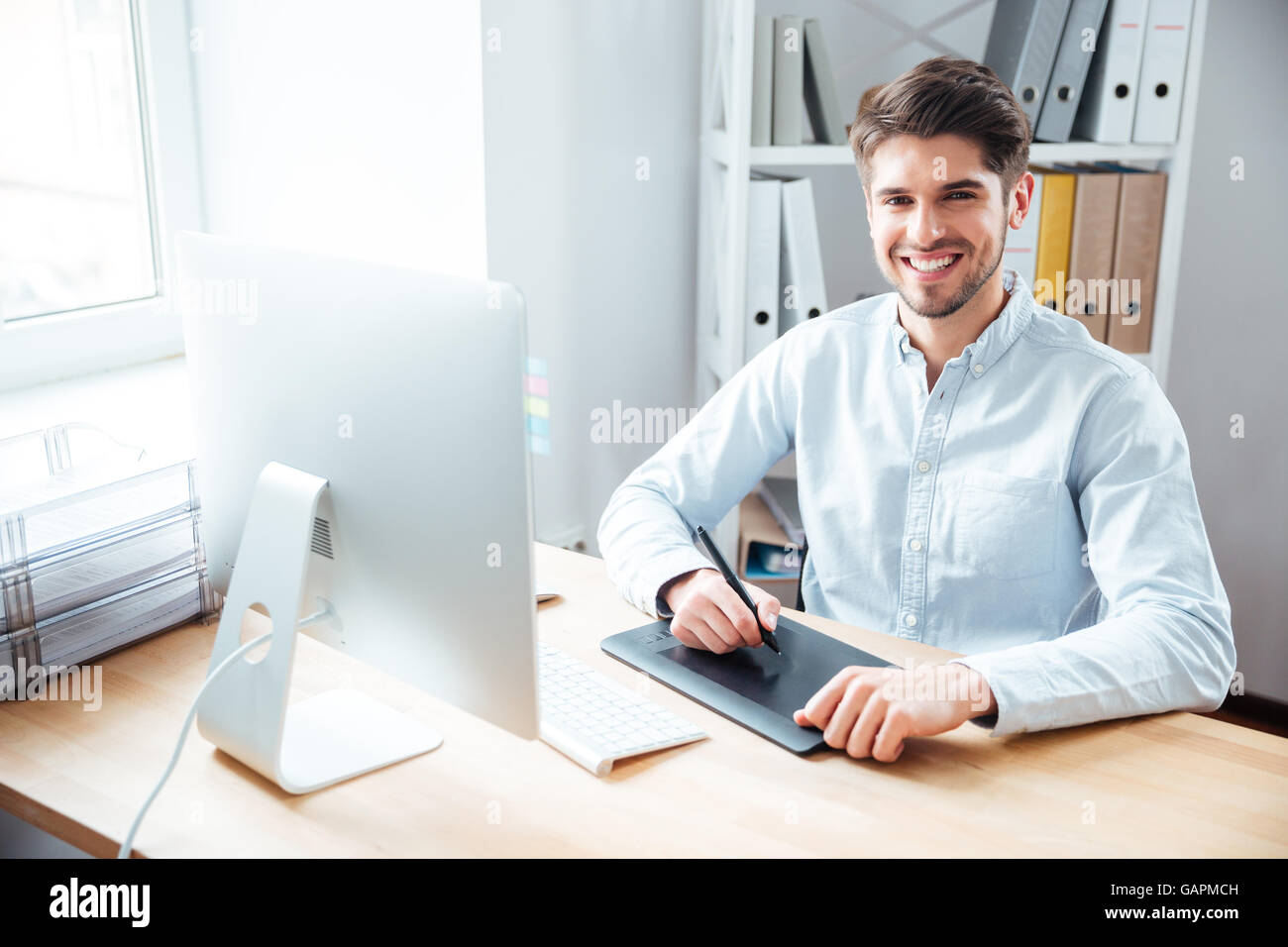 Portrait of smiling young man designer working and using graphic tablet ...