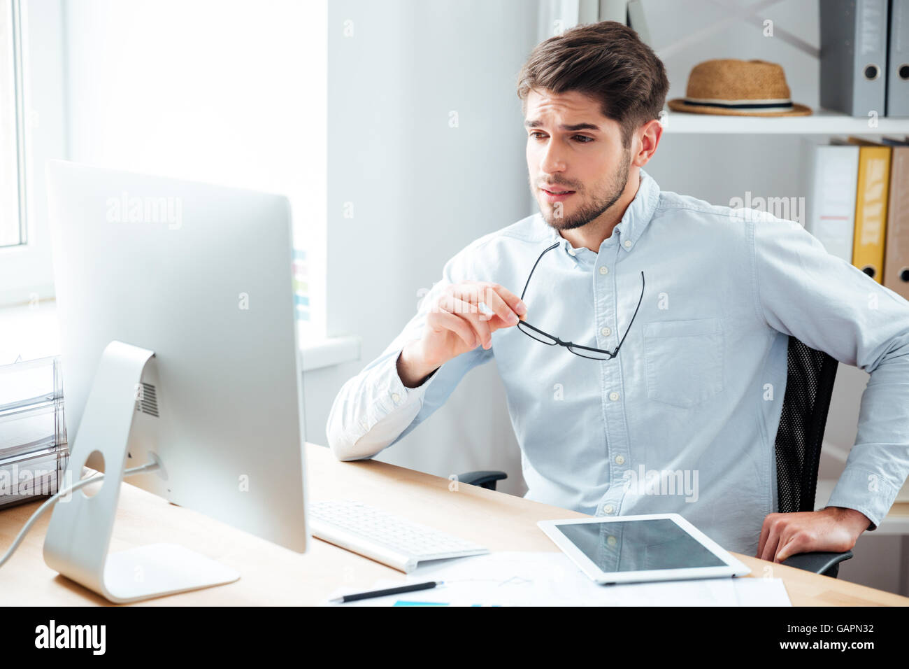 Pensive young handsome businessman holding eyeglasses and looking at ...