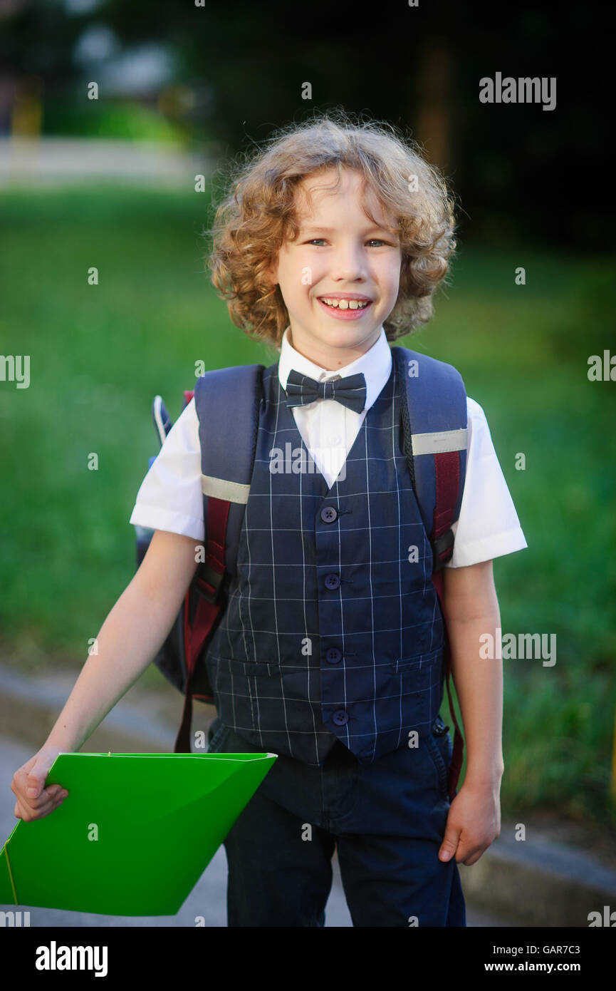 Little smart first grader in the school yard. Schoolboy looking at ...