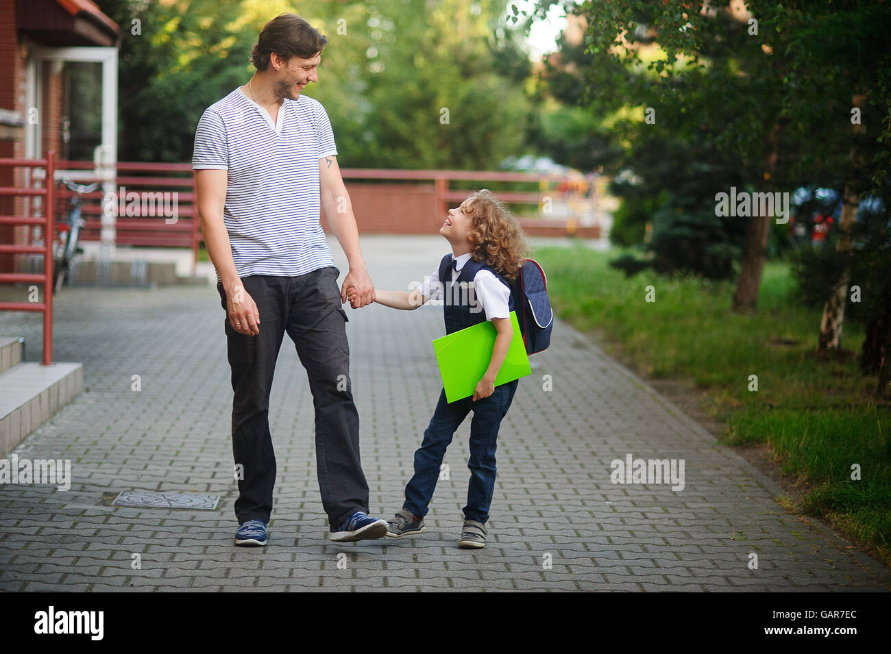 Dad walks to school his son. The tall man holds the hand of a little ...