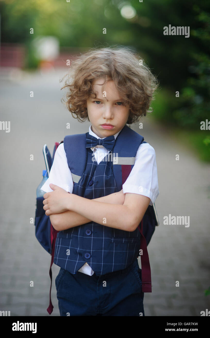 Little schoolboy stands in the school yard with an angry expression on ...