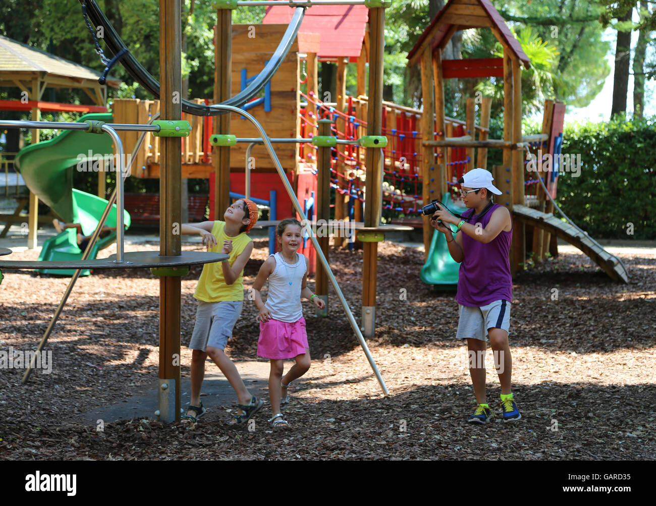 three children enjoy the playground in summer. The older guy doing a ...