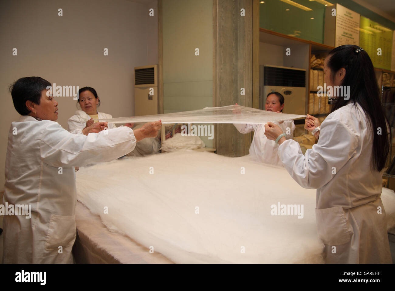Women workers stretch a very thin silk sheet to lay it over other ones ...