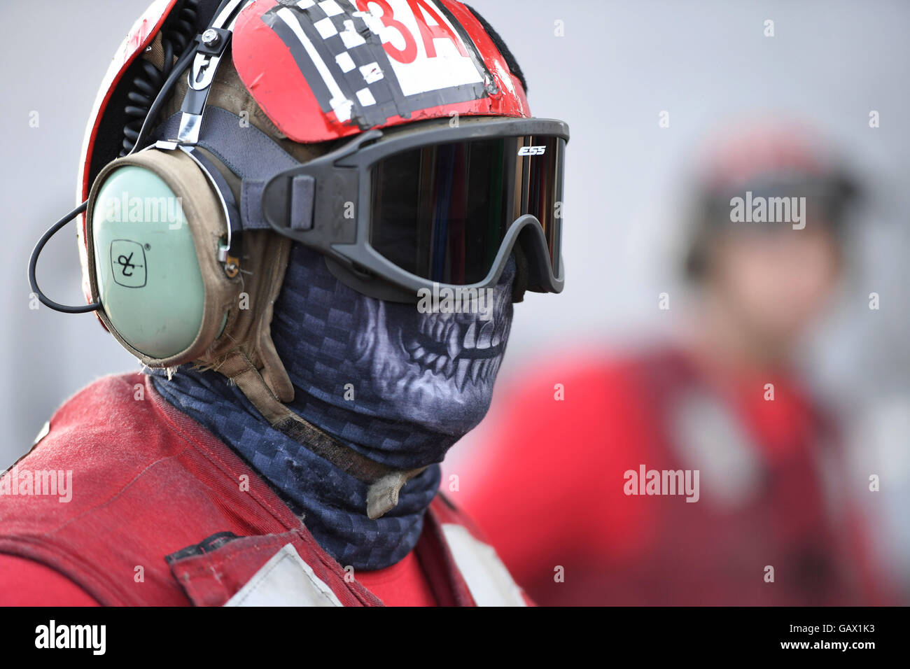 An aviation ordnanceman wears a mask on the deck of aircraft carrier ...