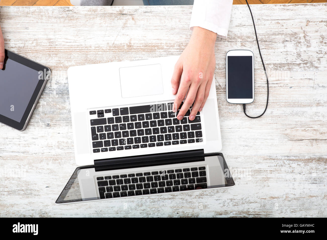 A young man using his laptop computer and various other devices on a ...