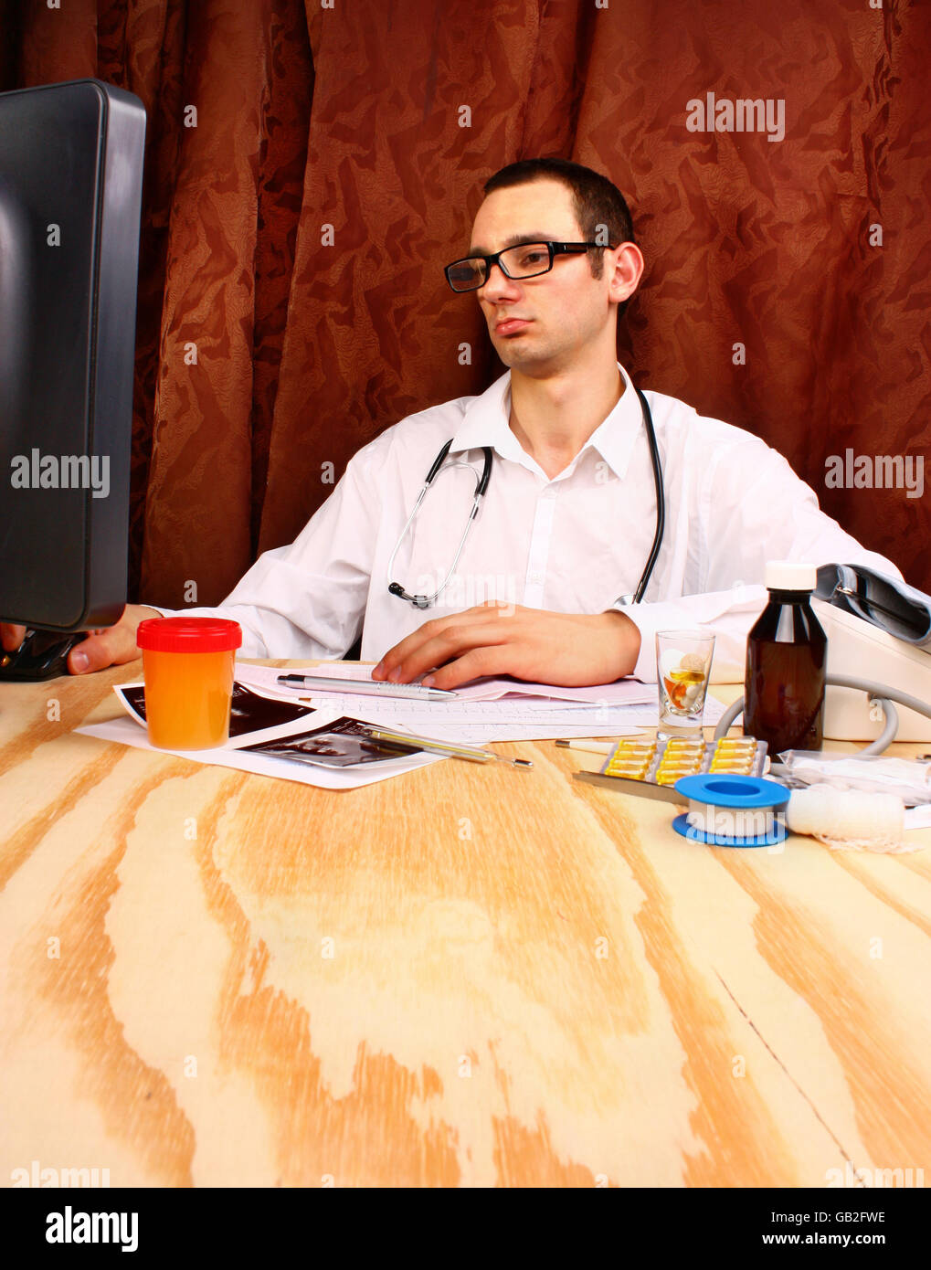 Male doctor with report looking at computer monitor at desk in medical ...