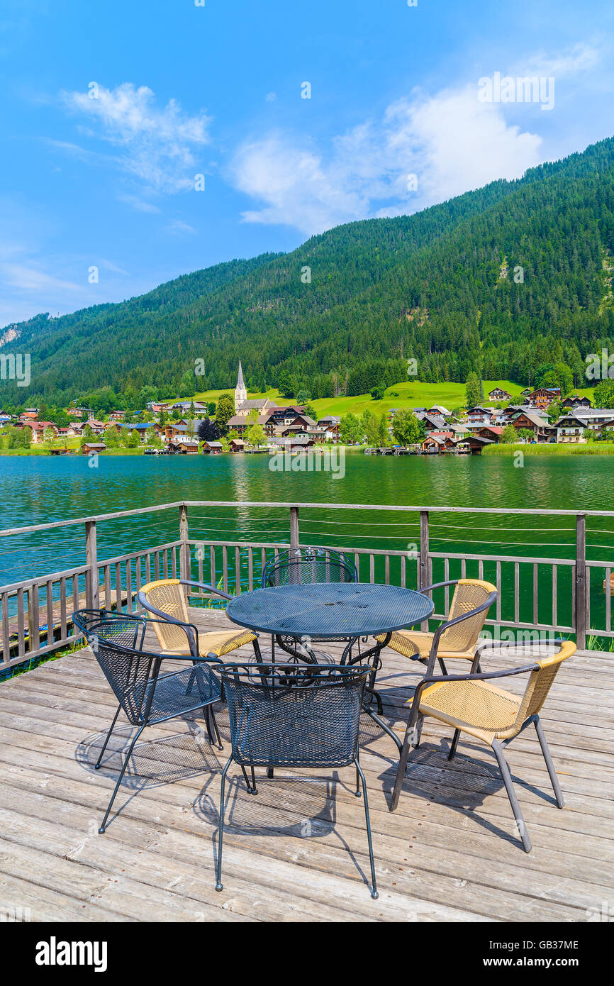 Table with chairs on wooden deck and view of green water Weissensee ...