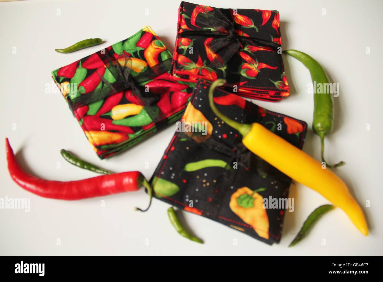 Assorted hot chillies scattered on chilli-patterned fabric coasters ...