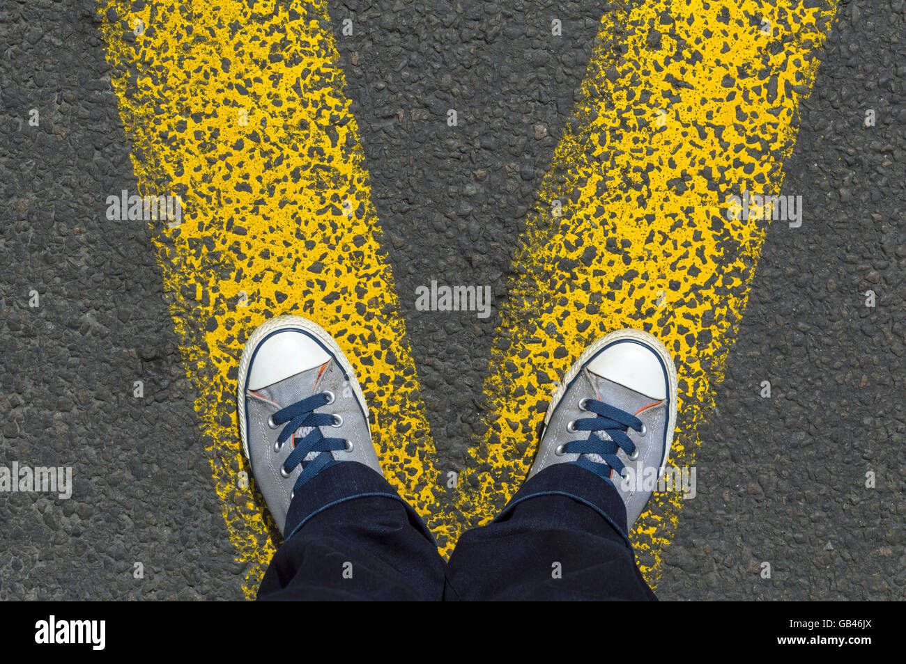 Sneakers stand on asphalt pavement with the yellow road marking lines ...