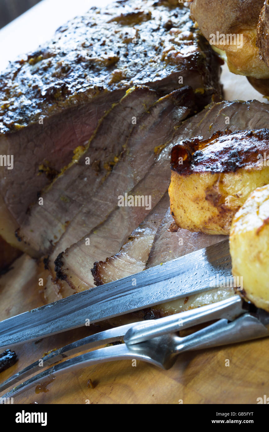 Freshly cooked English Roast Beef partially carved on a wooden board ...