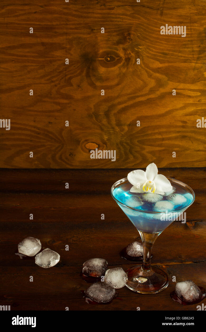 Blue cocktail in a martini glass with white orchid, vertical, copy ...